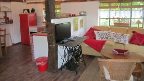 Uma sala de estar aconchegante com uma geladeira vermelha, uma televisão e uma mesa de madeira.