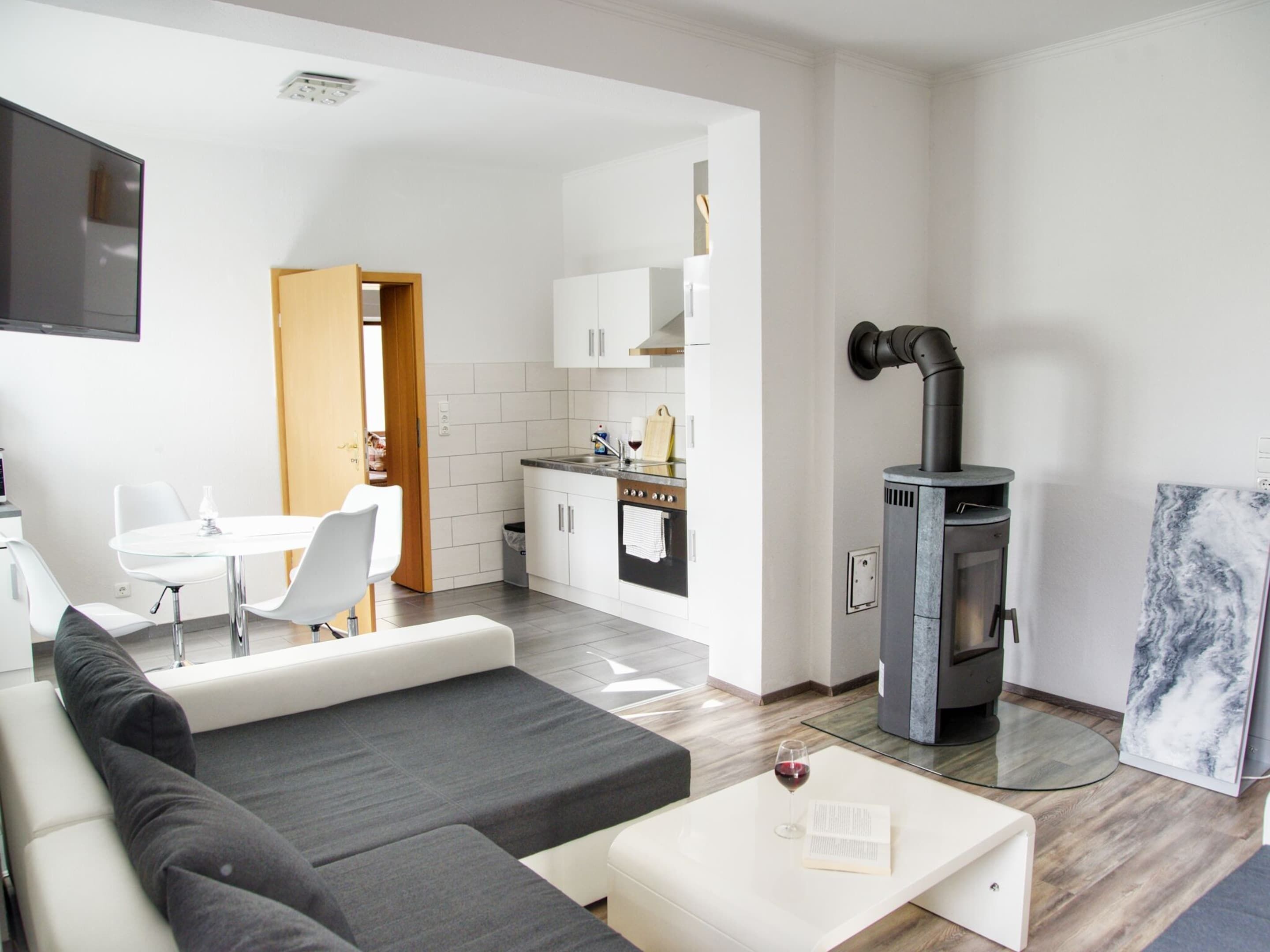 Uma sala de estar moderna com um sofá, uma mesa de centro de vidro e uma área de cozinha com fogão e armários.