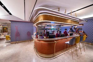 Uma área de bar moderna com balcão curvo, banquetas e um espaço de estar com mesas e cadeiras.