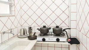 Uma cozinha com fogão a gás, duas panelas, uma frigideira e uma pia.
