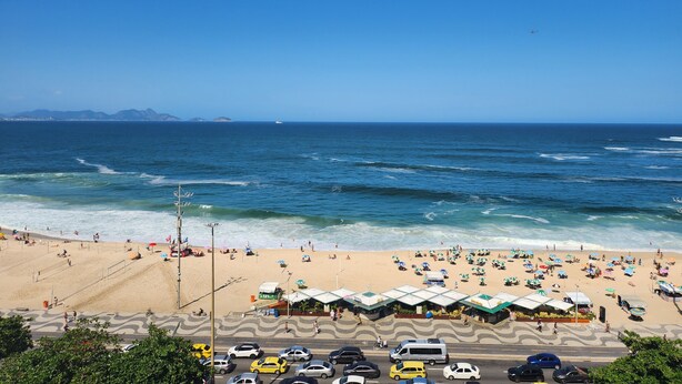 Uma praia com guarda-sóis, uma estrada e carros.