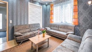 Uma sala de estar moderna com sofás cinza, uma mesa de centro de madeira e cortinas estampadas.