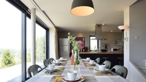 Uma sala de jantar com mesa posta para quatro pessoas, um vaso com flores e vista para o exterior.