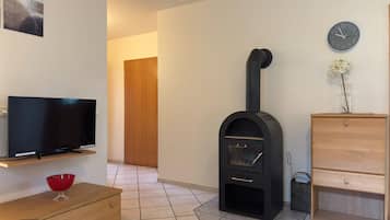Uma sala de estar com televisão, um armário de madeira, uma lareira a lenha preta e um relógio na parede.