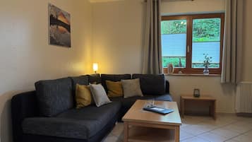 Sala de estar com sofá escuro, mesa de centro de madeira, luminária e janela com cortinas.