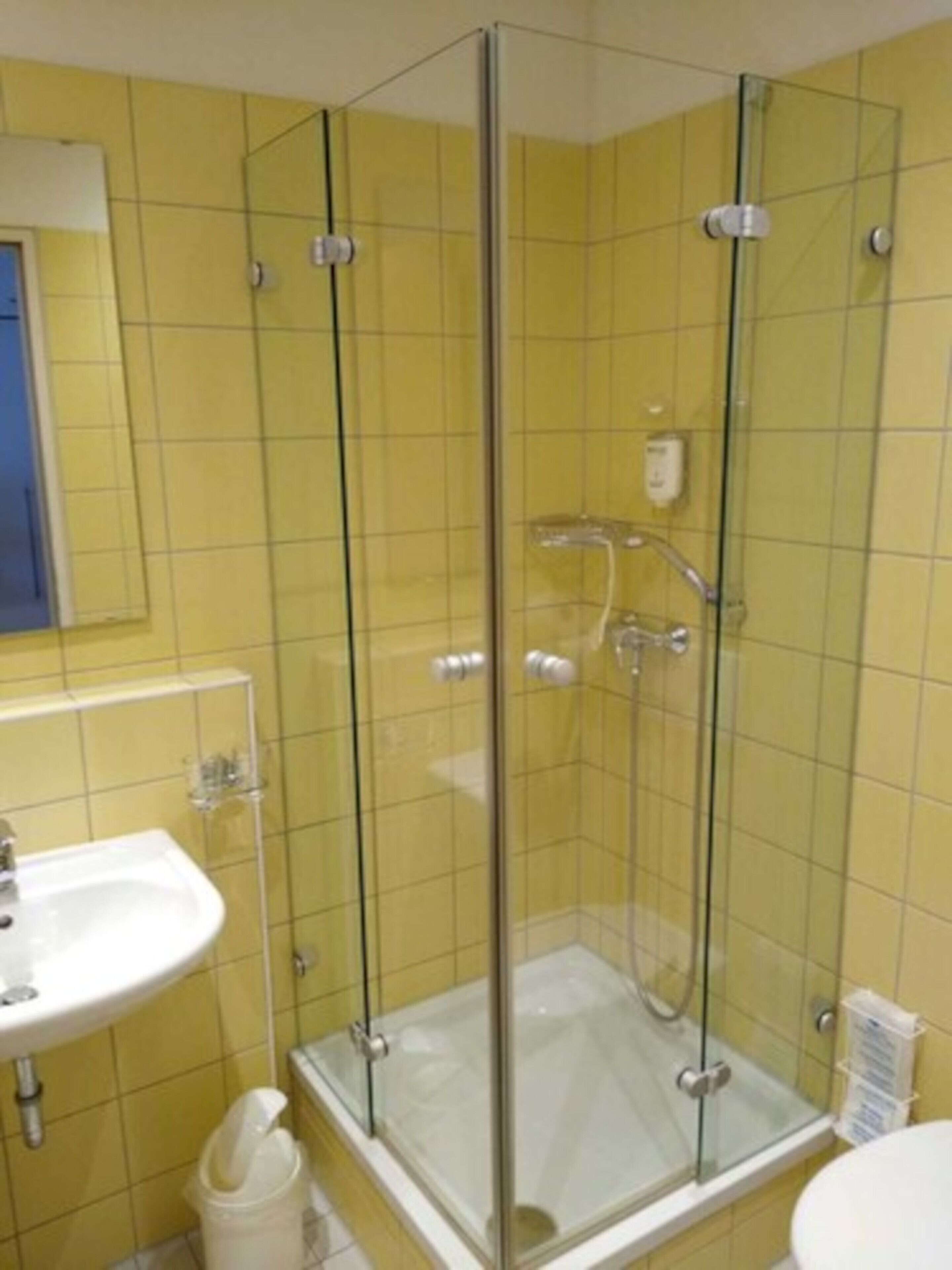 Casa de banho com azulejos amarelos, cabine de duche com vidro, lavatório e sanita.