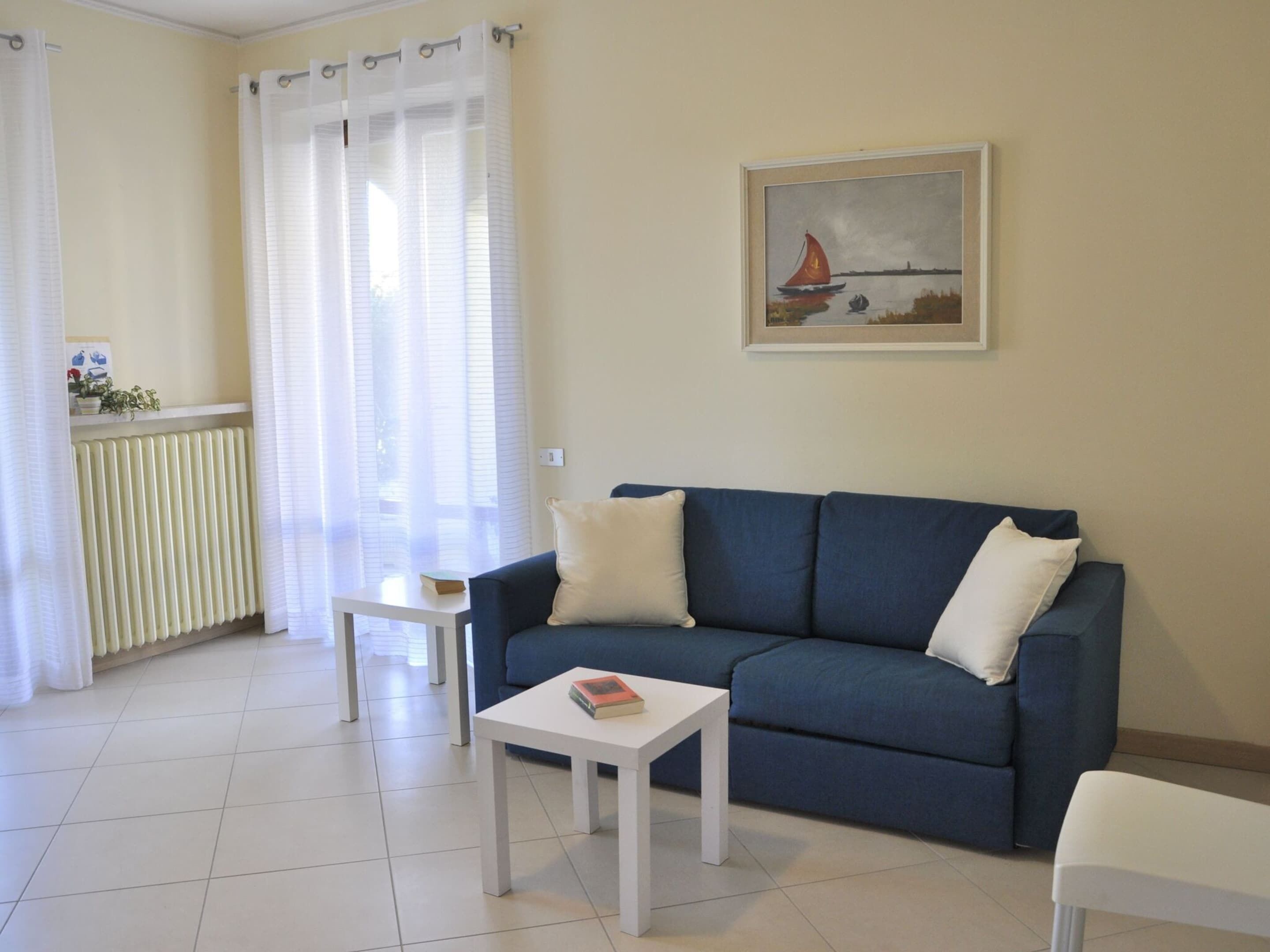 Uma sala de estar com um sofá azul, uma mesa de centro branca e um quadro de um veleiro na parede.