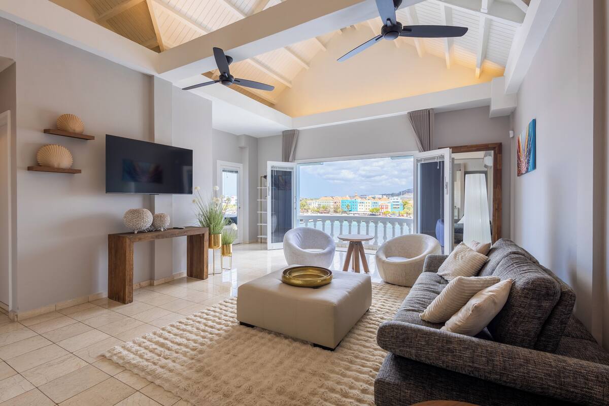 Uma sala de estar moderna com televisão de tela plana, sofá, mesa de centro e varanda com vista.