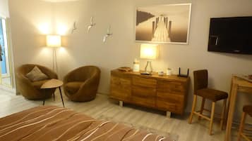 Quarto de hotel com cama, duas poltronas, cômoda de madeira, escrivaninha com cadeira, televisão de tela plana, obras de arte na parede e luminária.