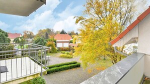 Uma varanda com vista para um pátio, um pequeno jardim e um edifício com telhado vermelho.