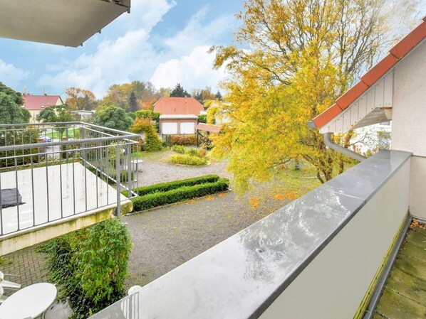Uma varanda com vista para um pátio, um pequeno jardim e um edifício com telhado vermelho.