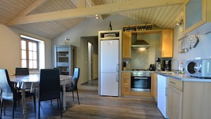 Cozinha ampla com armários de madeira, área de jantar com mesa e cadeiras, e vista para o cômodo vizinho.