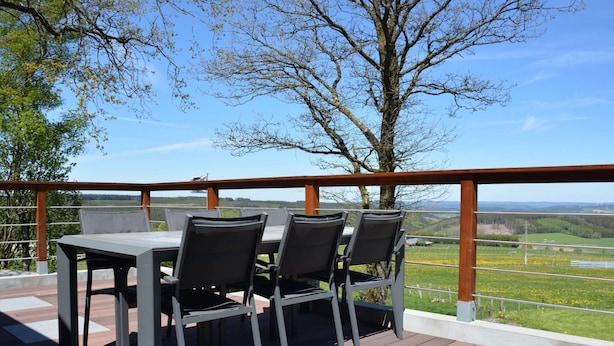 Um deck externo com mesa e cadeiras, com vista para uma paisagem deslumbrante.