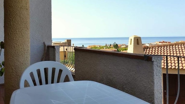 Uma varanda com mesa e cadeiras, oferecendo vista para a costa, com edifícios e o mar.