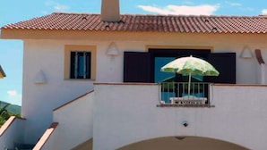 Um edifício de dois andares com varanda, telhado ladrilhado e um pequeno jardim.