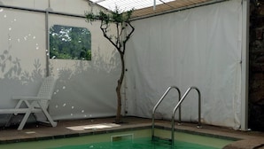 Piscina interna com uma árvore, uma cadeira e escadas de metal.