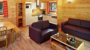 Interior de uma cabana de madeira com sala de jantar, dois sofás, uma mesa de centro e cozinha.