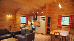 Interior acolhedor de uma cabana, com área de jantar, sofá e cozinha.
