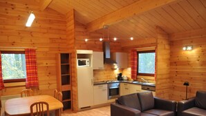 Interior de cabana de madeira com mesa de jantar, cadeiras, sofá e cozinha, incluindo micro-ondas e fogão.