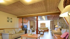 Uma sala de estar ampla, com teto de madeira, televisão e lareira.