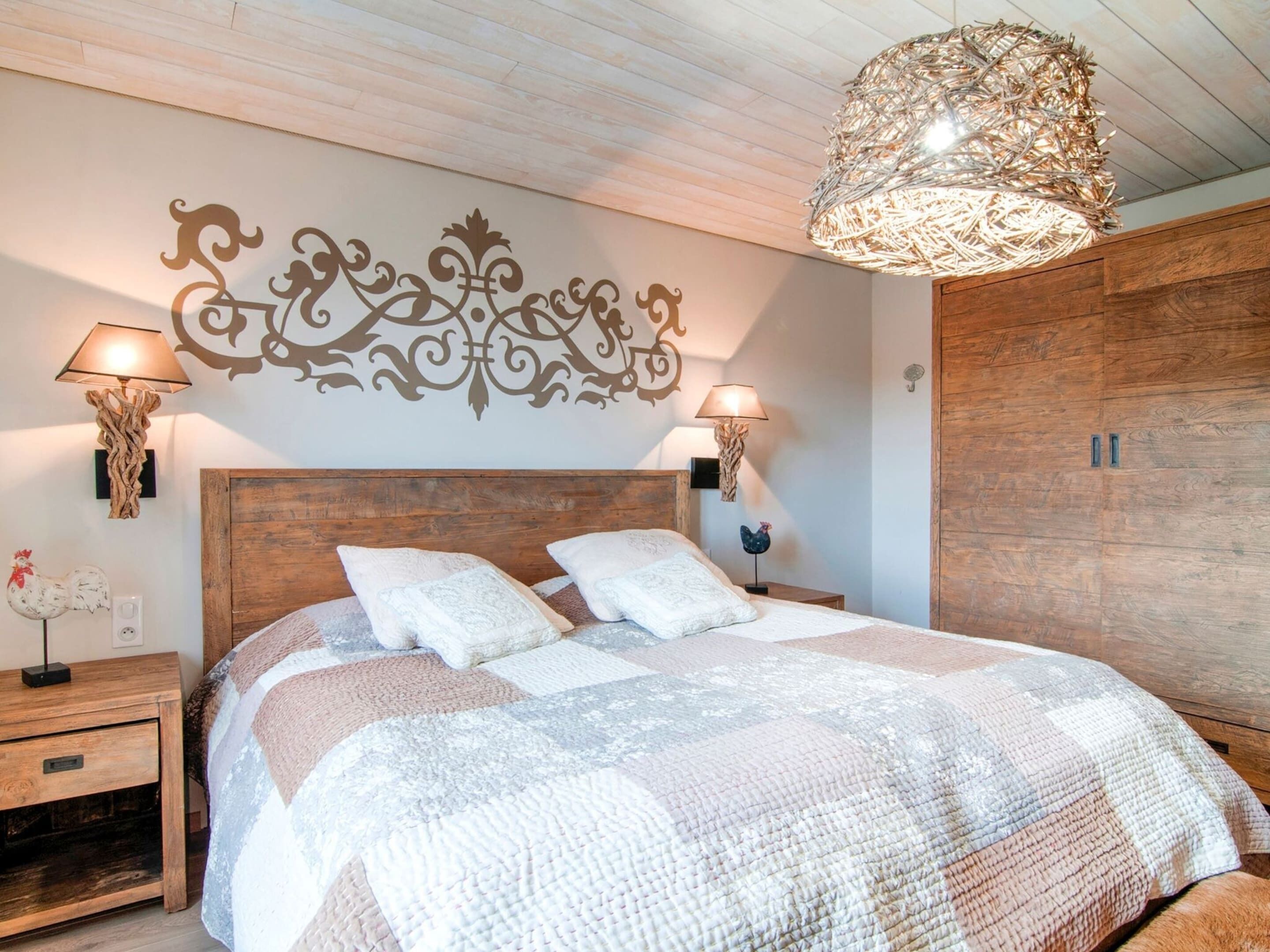 Quarto com uma cama grande, duas luminárias de cabeceira, um objeto decorativo na parede e um guarda-roupa de madeira.