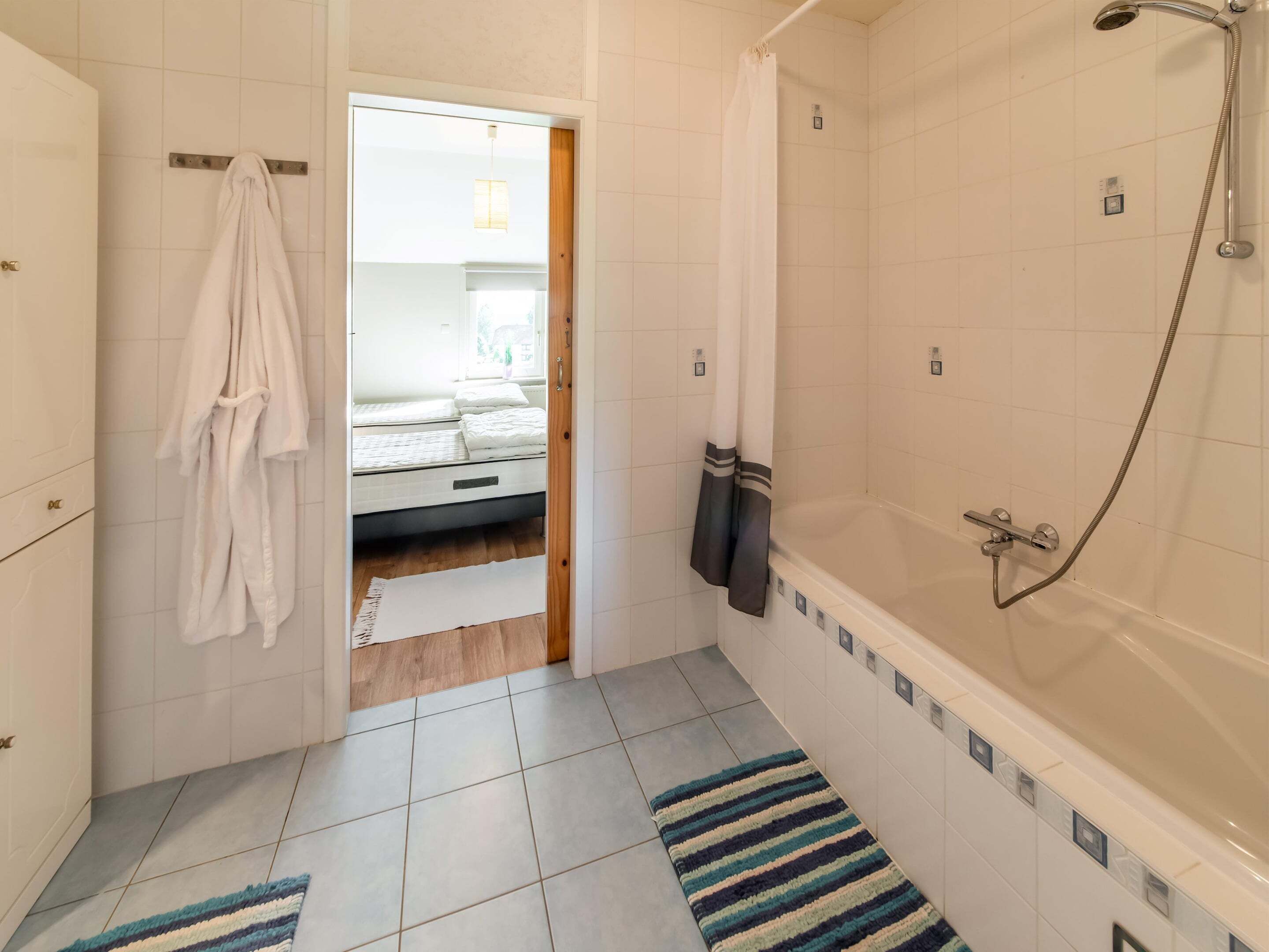 Casa de banho com chuveiro, banheira e uma cama visível no quarto adjacente.