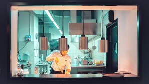 Um chef em uma cozinha profissional com eletrodomésticos de aço inoxidável, luminárias pendentes e um espaço de trabalho limpo e organizado.