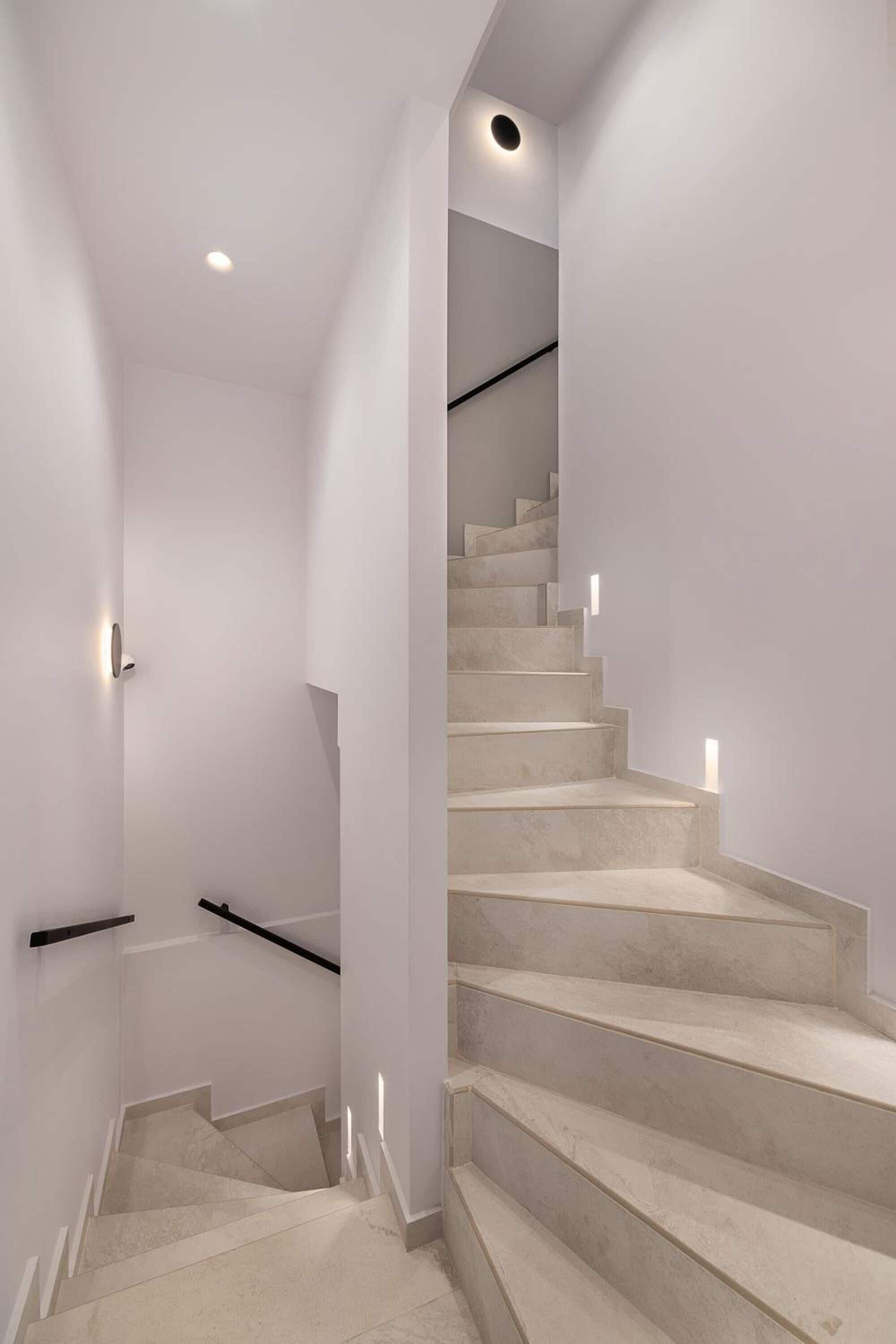 Escadaria moderna com design minimalista, piso e paredes em tons claros, e iluminação embutida ao longo dos degraus.
