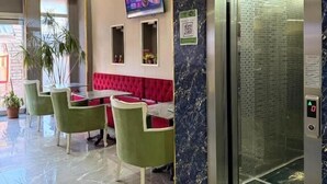 Um hall de entrada com piso de mármore, cadeiras verdes, um balcão vermelho, uma televisão e um elevador.