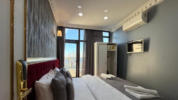 Quarto de hotel com cama grande, guarda-roupa, espelho, janela com cortinas e ar condicionado.