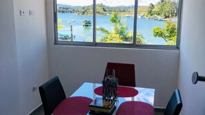 Uma área de refeições com mesa e cadeiras, vista para um lago com barcos e uma cadeira vermelha.