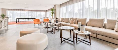 Um hall de hotel moderno com sofá, pufes e mesas.