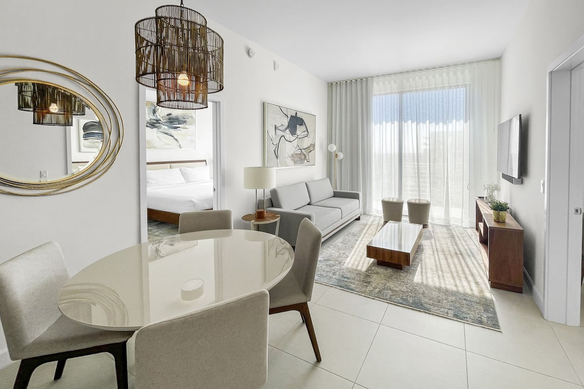 Quarto de hotel moderno com área de refeições, sofá, televisão e obras de arte nas paredes.
