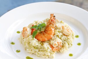 Prato de camarão com arroz, decorado com uma folha de manjericão e molho verde.