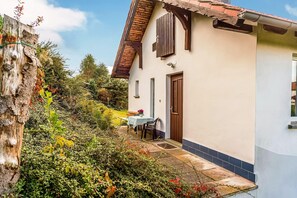 Uma casa com fachada branca, persianas de madeira e um pátio com telhado e mesa com cadeiras.