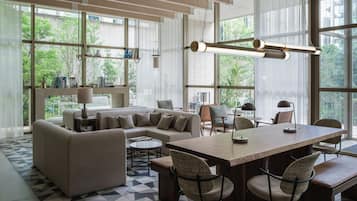 Uma sala de estar moderna com um amplo sofá modular, uma mesa de jantar com cadeiras e uma mesa de centro. Janelas grandes oferecem luz natural e vista para o verde lá fora.