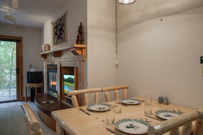 Uma sala de jantar com uma mesa de madeira posta para quatro pessoas, lareira e televisão.