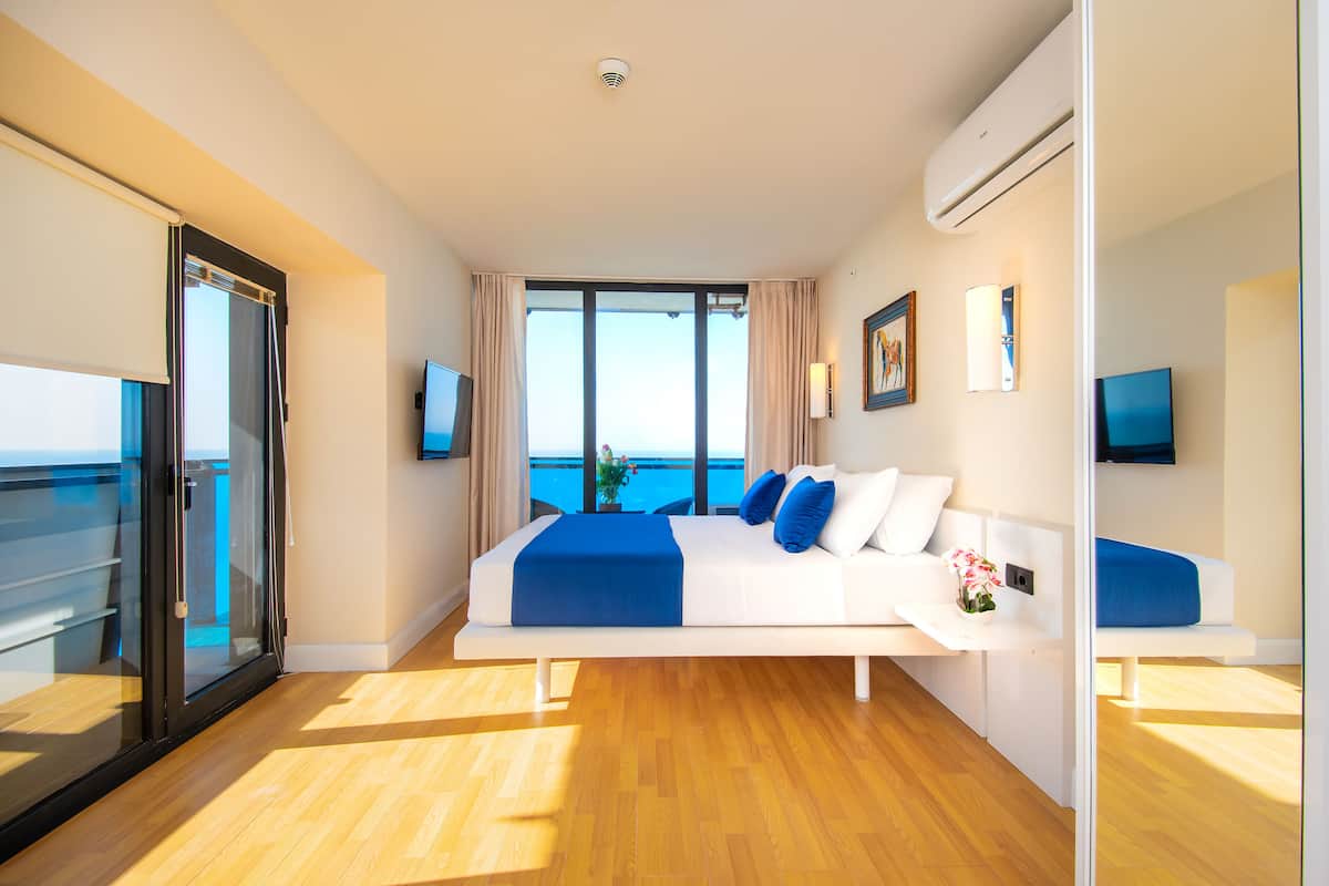 Quarto de hotel moderno com uma cama grande, varanda e vista para o mar.