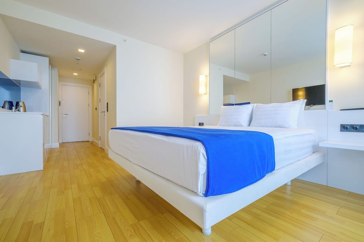 Quarto de hotel moderno com uma cama grande, uma mesinha de cabeceira, um espelho e um guarda-roupa.