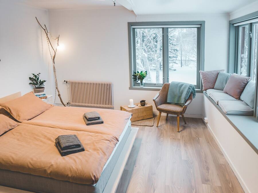 Um quarto aconchegante com uma cama grande, uma poltrona, um assento à janela e um radiador.