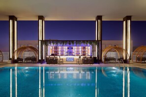 Uma área de bar à beira da piscina, com balcão, assentos e piscina.