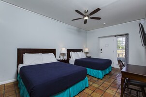 Quarto de hotel com duas camas, um ventilador de teto, uma escrivaninha e uma televisão.