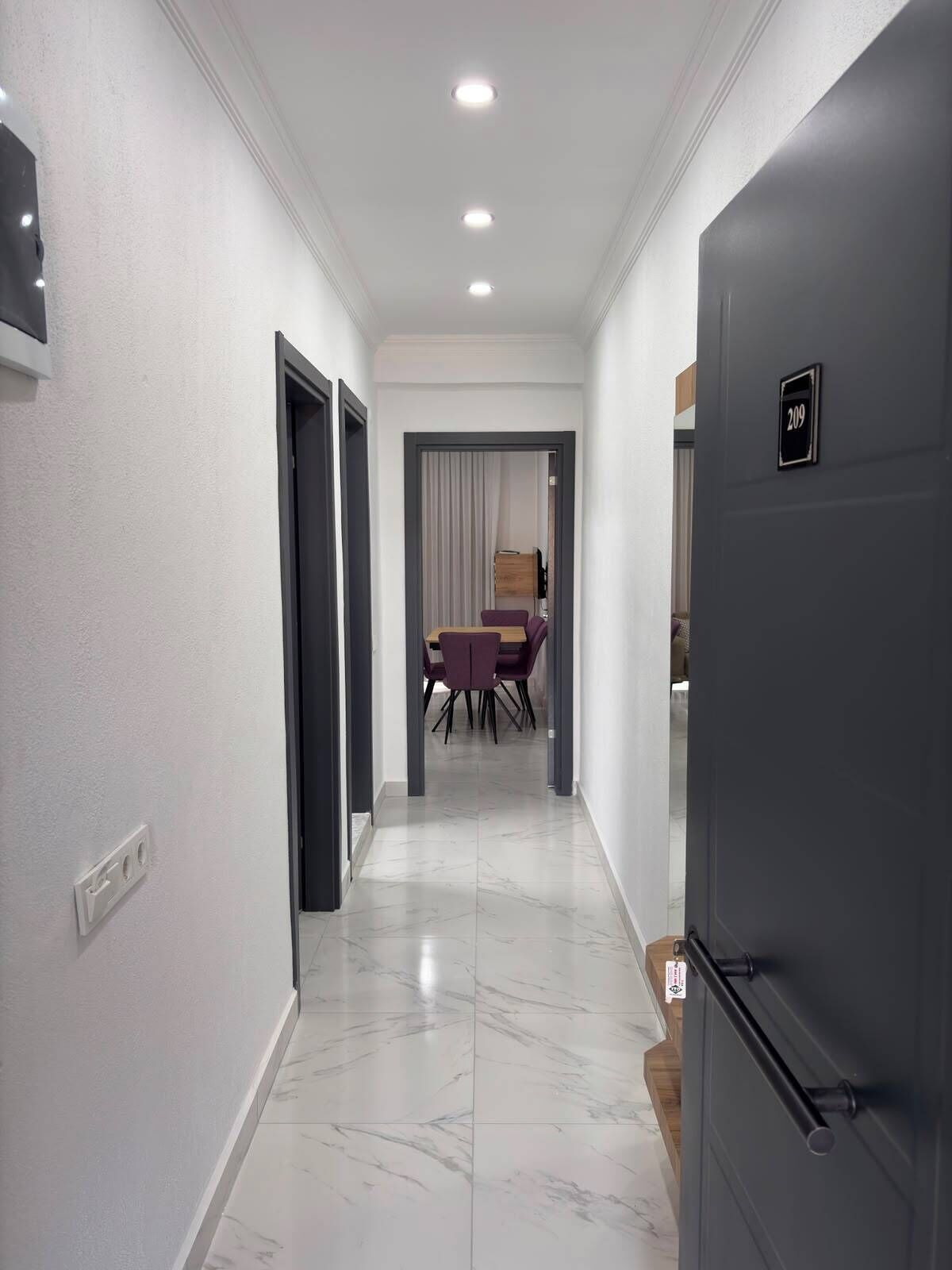 Um corredor com área de refeições, uma porta numerada e um interruptor de luz.
