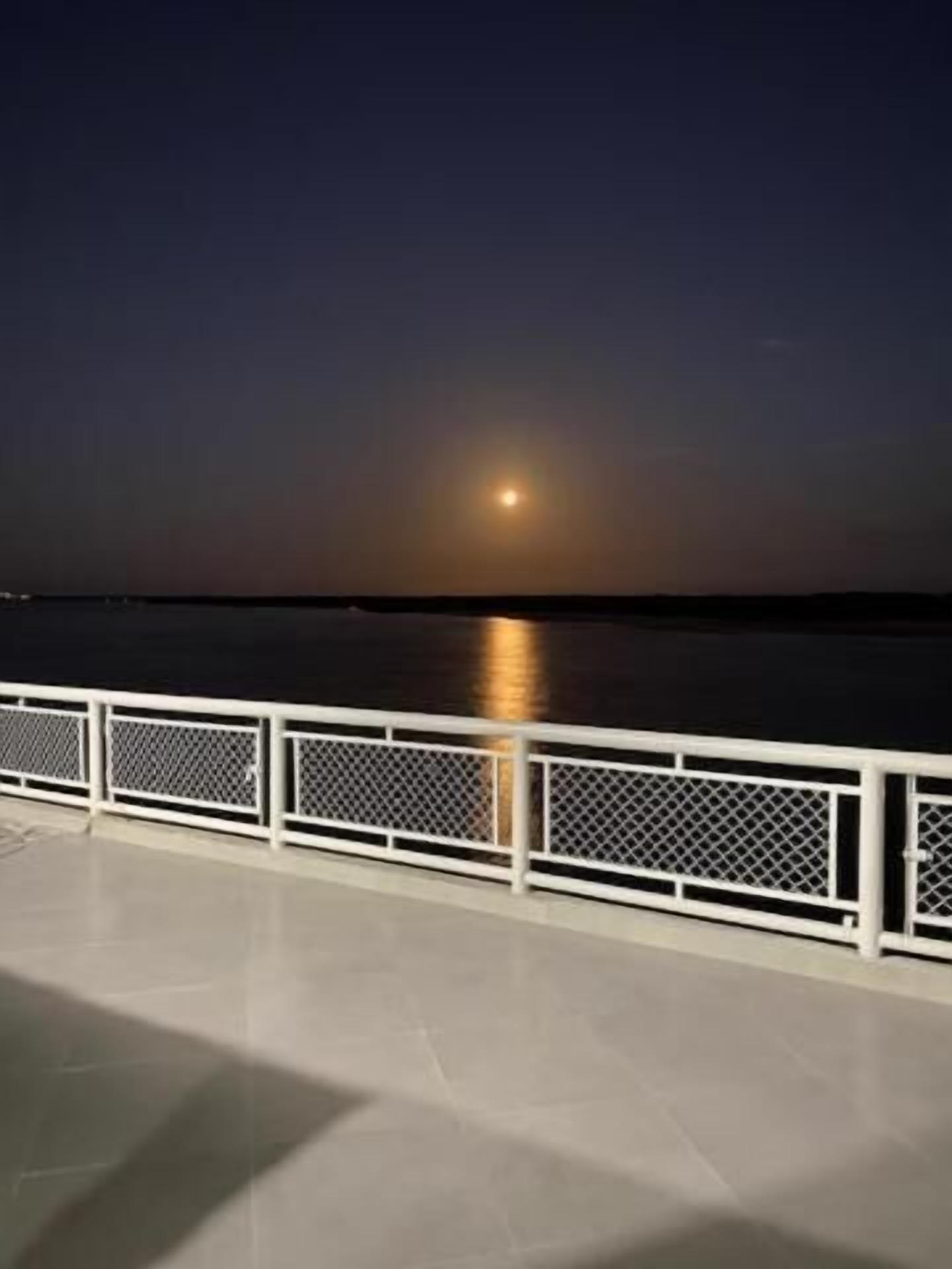 Vista noturna de um calçadão à beira-mar, com guarda-corpo branco e mar calmo.