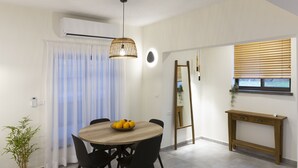 Uma área de refeições com uma mesa redonda, cadeiras pretas, uma tigela de madeira com frutas e um lustre.