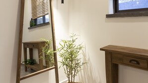 Um quarto com escrivaninha de madeira, um espelho apoiado na parede, um vaso de planta e uma janela com persianas.