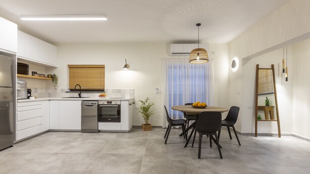 Cozinha moderna com armários brancos, forno embutido e área de jantar com mesa redonda e cadeiras.