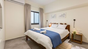 Quarto com cama, janela com cortinas, mesa de cabeceira com planta e obra de arte na parede.