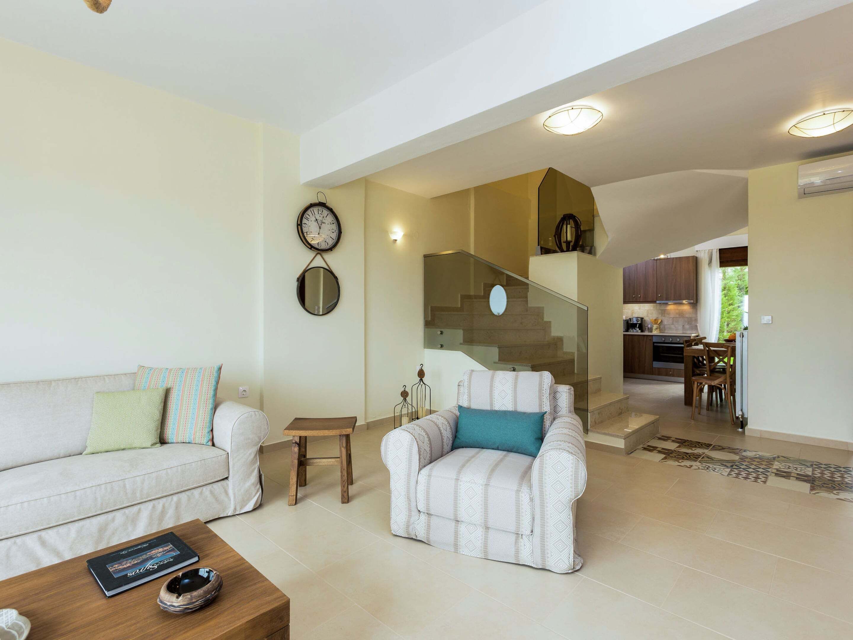 Sala de estar com sofá, poltrona, mesa de centro e escada que leva a uma cozinha.