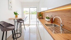 Cozinha moderna com bancada de madeira, pia de aço inoxidável e um pequeno espaço de refeições com duas cadeiras e uma mesa.